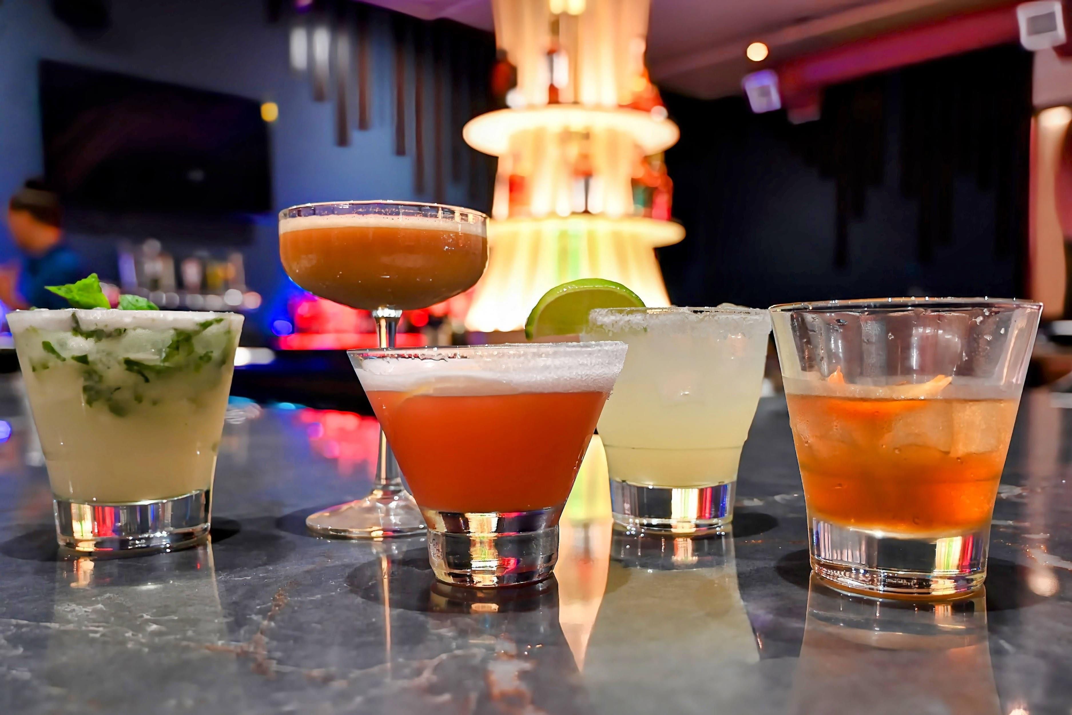 Quatro coquetéis em um balcão de bar, com uma luz decorativa ao fundo.