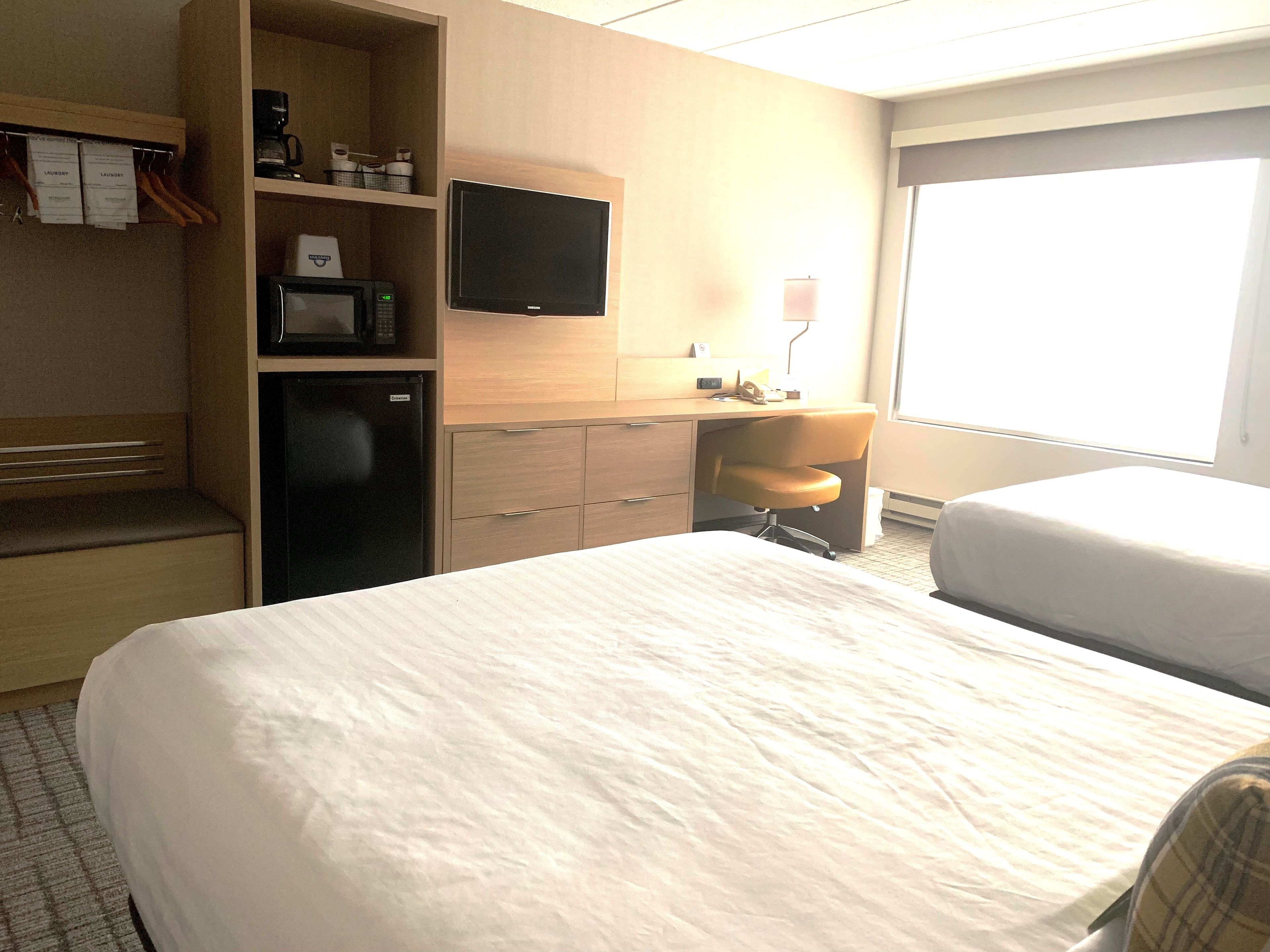 Quarto de hotel com cama, escrivaninha e cadeira, micro-ondas, televisão e janela com vista.