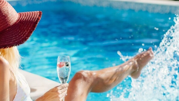 Uma pessoa relaxando em uma piscina com um copo de bebida.