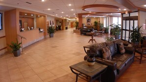 Um lobby amplo com balcão de recepção, área de estar com assentos de couro e plantas em vasos.