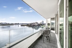 Uma varanda com vista para um rio e paisagem urbana, com uma mesa e cadeiras.