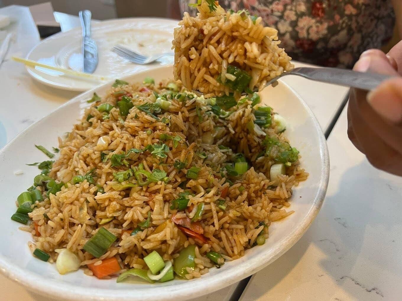 Um prato de arroz frito com legumes e um garfo.