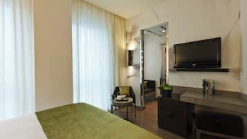 Quarto de hotel com cama, escrivaninha, cadeira, televisão e uma pequena mesa com uma planta.