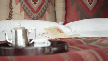 Uma cama com almofadas estampadas, um tabuleiro com bule de chá e um cardápio sobre a cama.