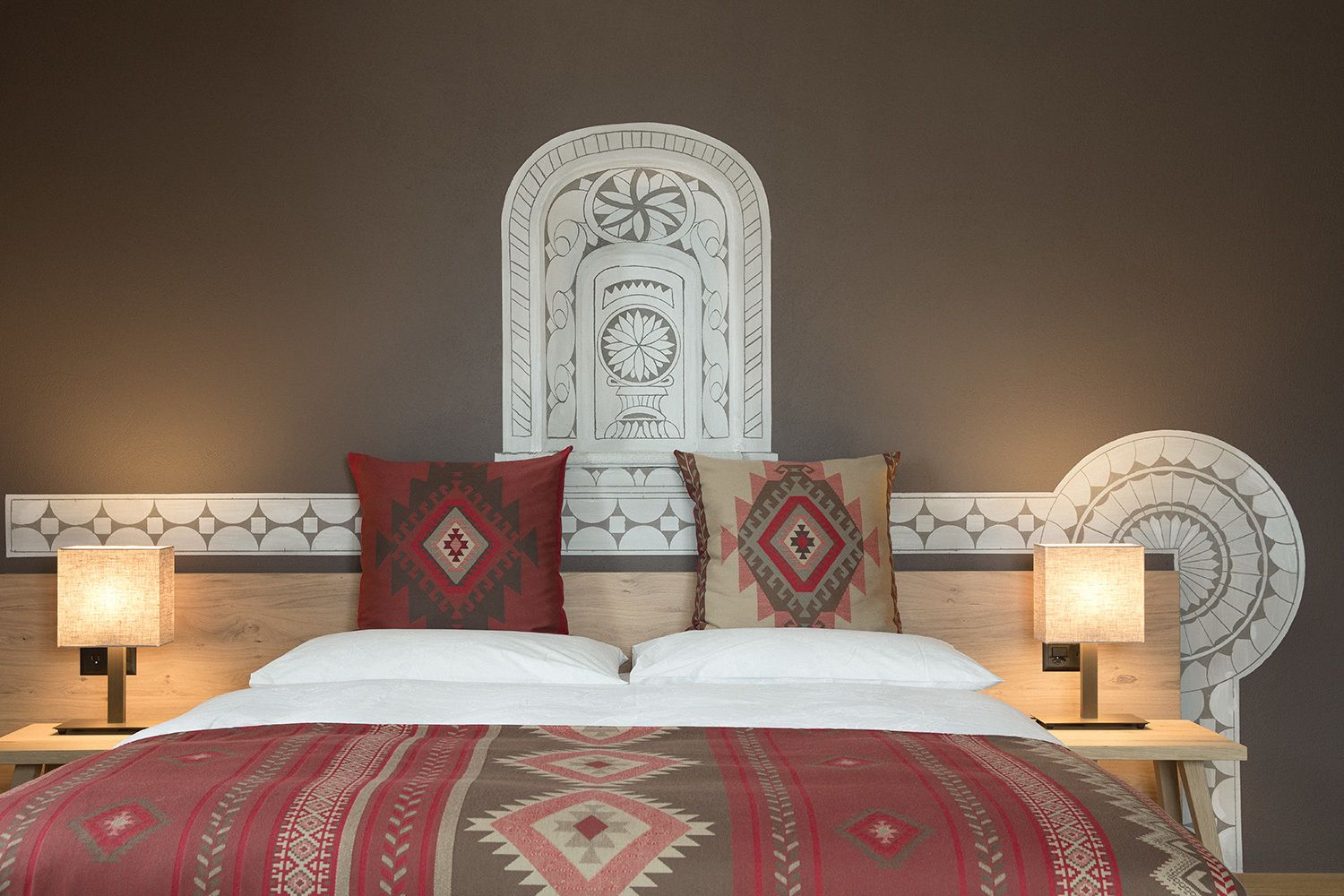 Uma cama com colcha estampada, duas almofadas com desenhos geométricos e cabeceira com padrões elaborados.