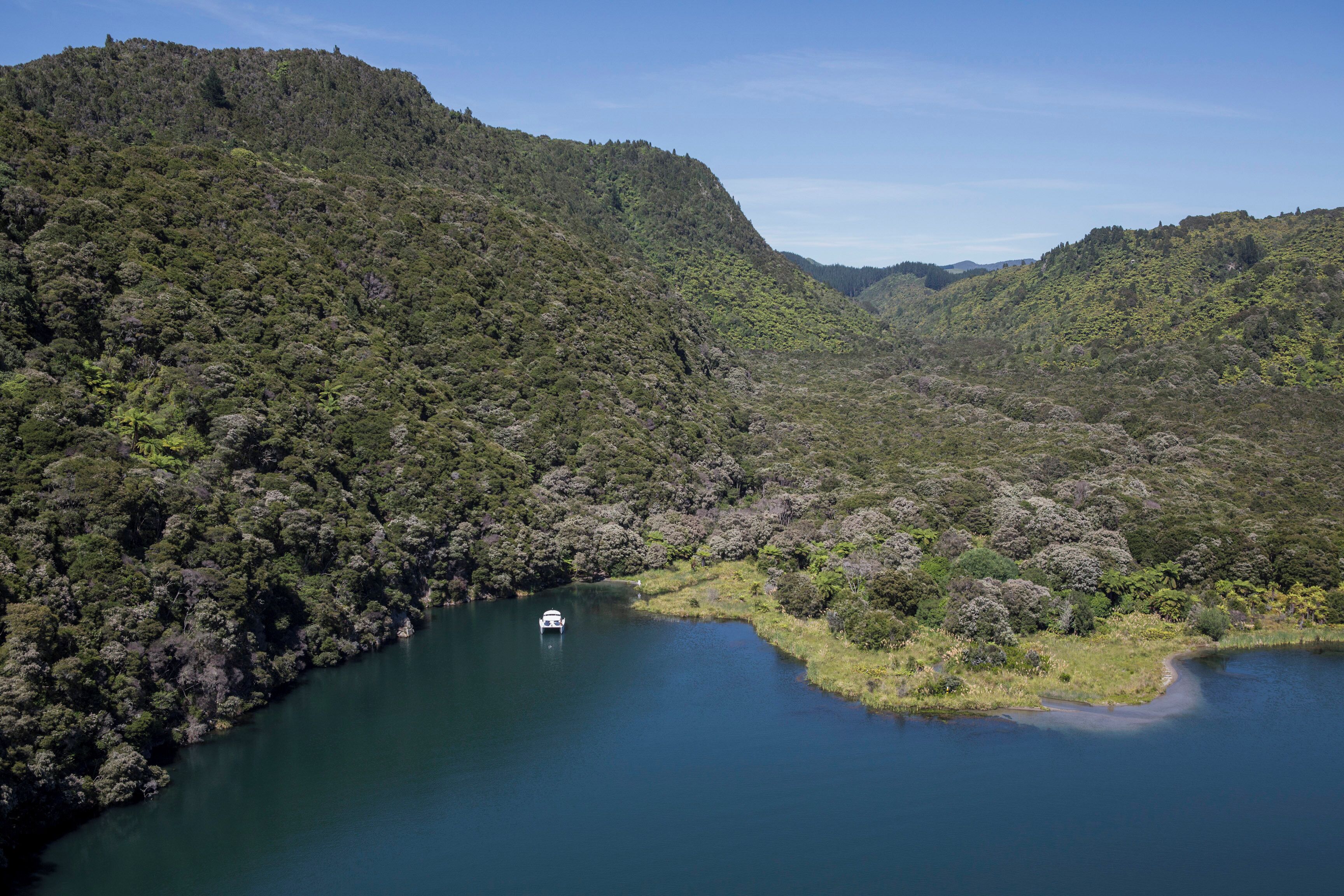 Um barco num lago calmo, rodeado por colinas verdes e exuberantes.