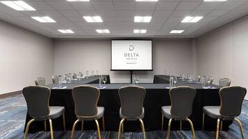 Uma sala de conferência com uma mesa comprida, seis cadeiras e uma tela de projetor exibindo "DELTA HOTELS MARRIOTT".