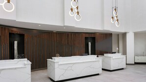 Uma área de recepção moderna com balcões de mármore, painéis de madeira e iluminação pendente.