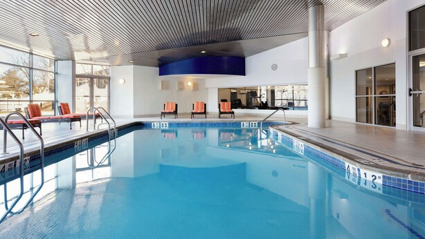 Piscina interna com água cristalina, cadeiras de descanso próximas e design moderno no teto.