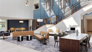 Um hall amplo com teto alto, uma escadaria e um espaço de estar com sofás e poltronas.