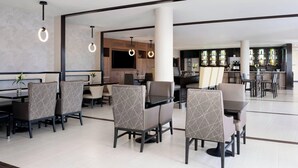 Uma área de jantar moderna com mesas e cadeiras altas, uma cozinha ao fundo e iluminação pendente.