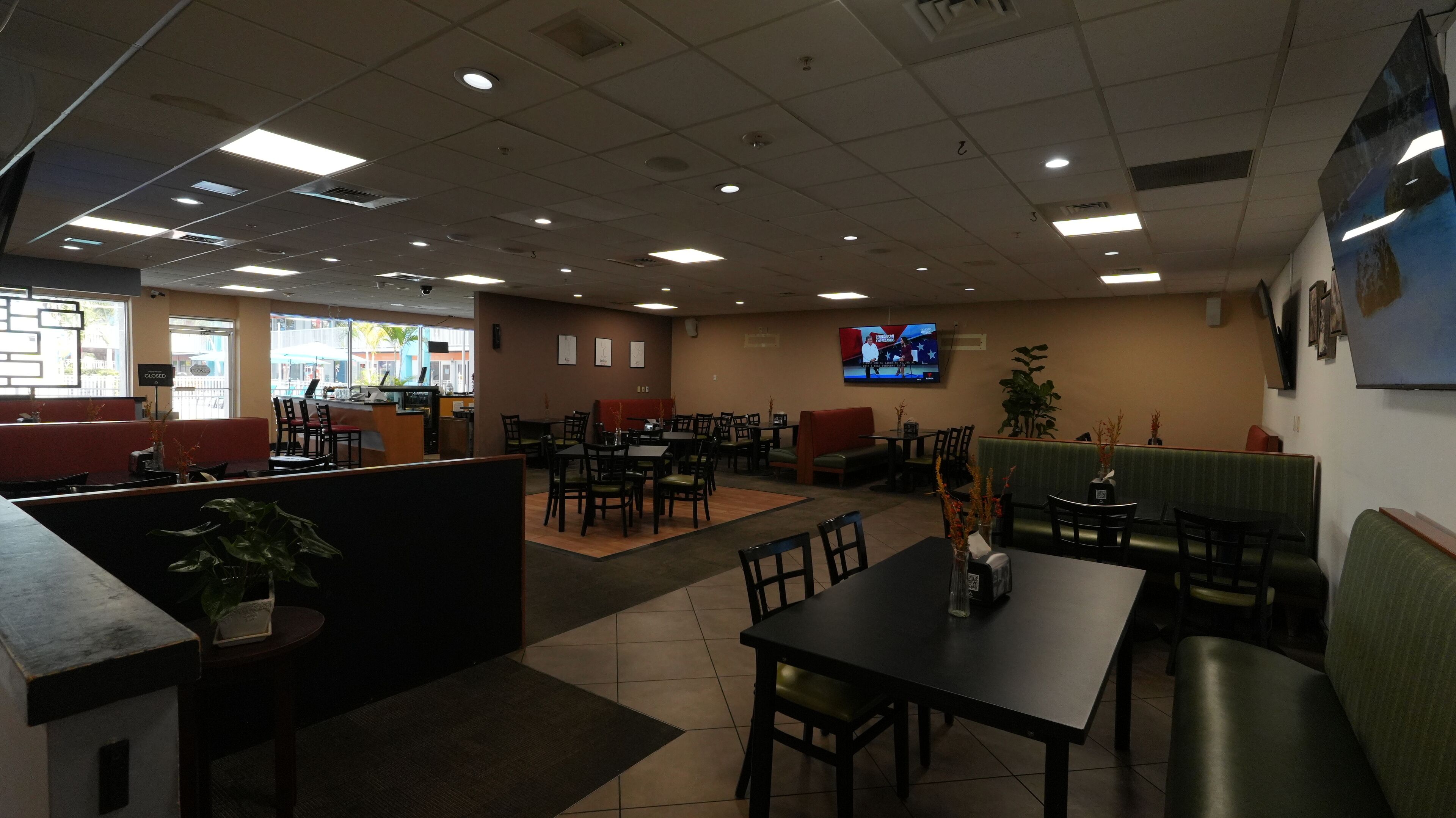 Interior de restaurante com cabines, mesas e uma tela de televisão.