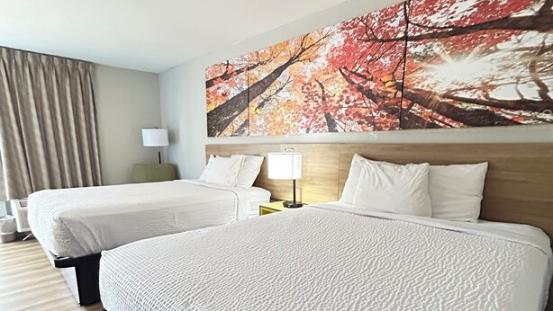 Quarto de hotel com duas camas, um mural grande na parede, uma luminária e uma cortina.