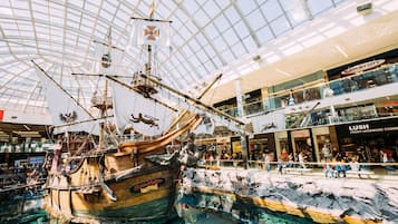 Um grande navio exposto em um átrio de shopping, com teto de vidro e cercado por compradores.