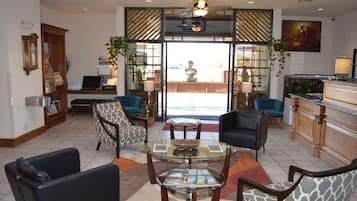 Um hall amplo com mesa de centro de vidro, assentos confortáveis, balcão de recepção e vista para o exterior.