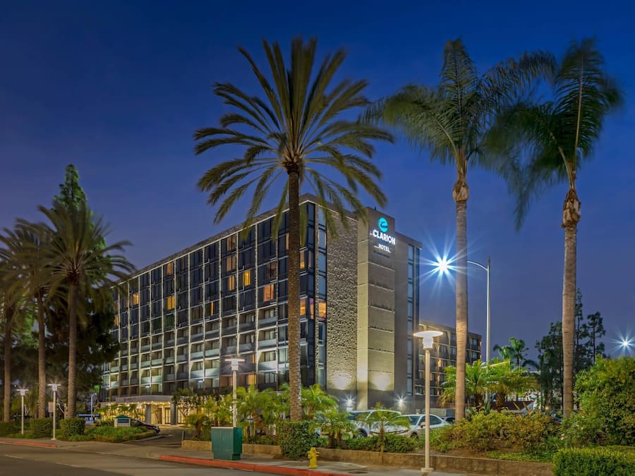Um hotel moderno com fachada de vidro, cercado por palmeiras e iluminado por postes de luz.