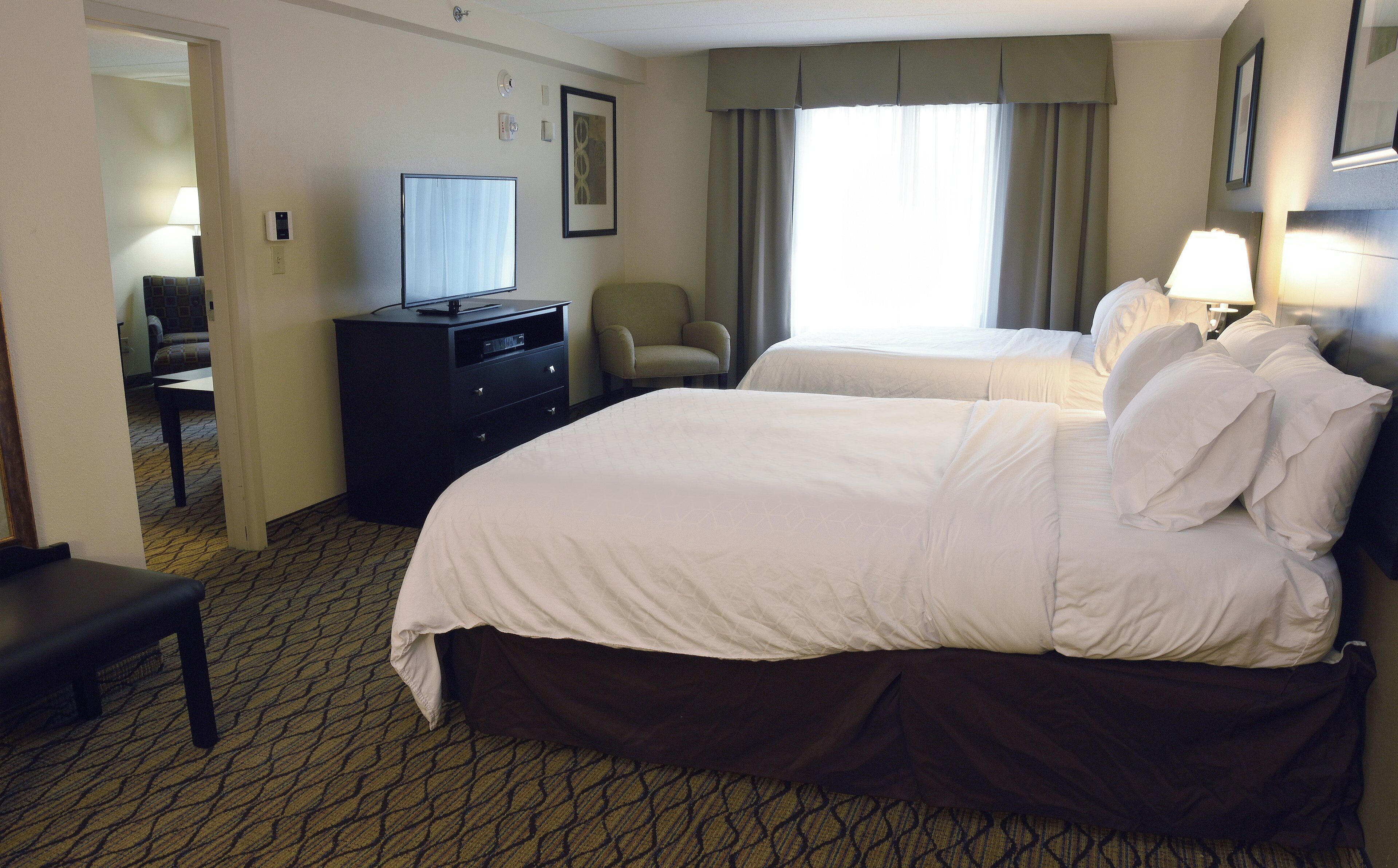 Quarto de hotel com duas camas, uma escrivaninha, uma cadeira, uma televisão e uma janela com cortinas.