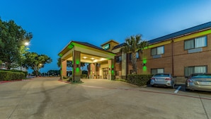 Entrada de hotel com área de estacionamento coberta, fachada de tijolos e dois carros estacionados.