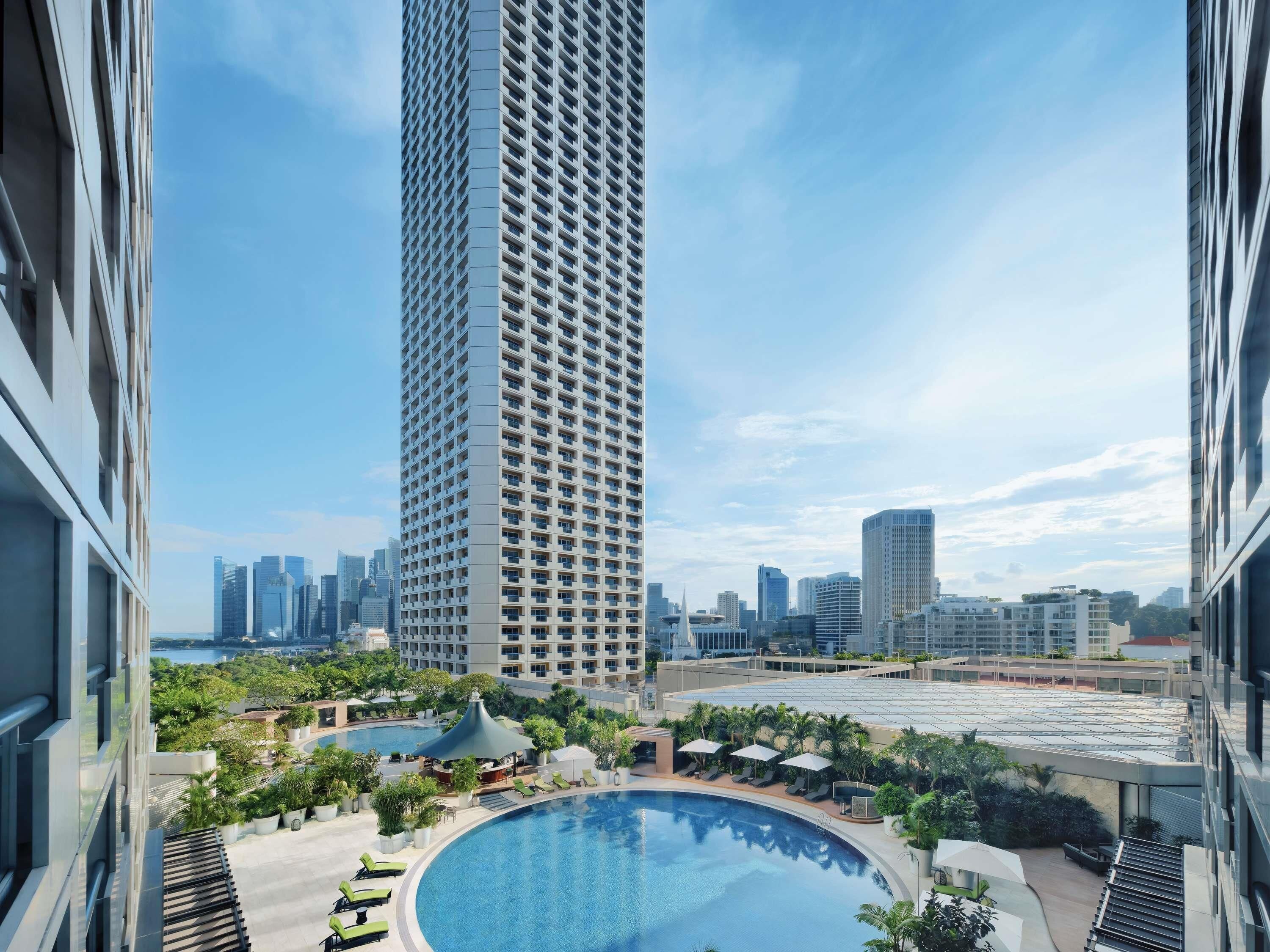 Um edifício alto com piscina e área de estar, cercado por vegetação e com vista para a paisagem urbana.