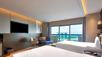 Quarto de hotel com uma cama grande, uma escrivaninha com cadeira, televisão na parede e vista para a cidade.