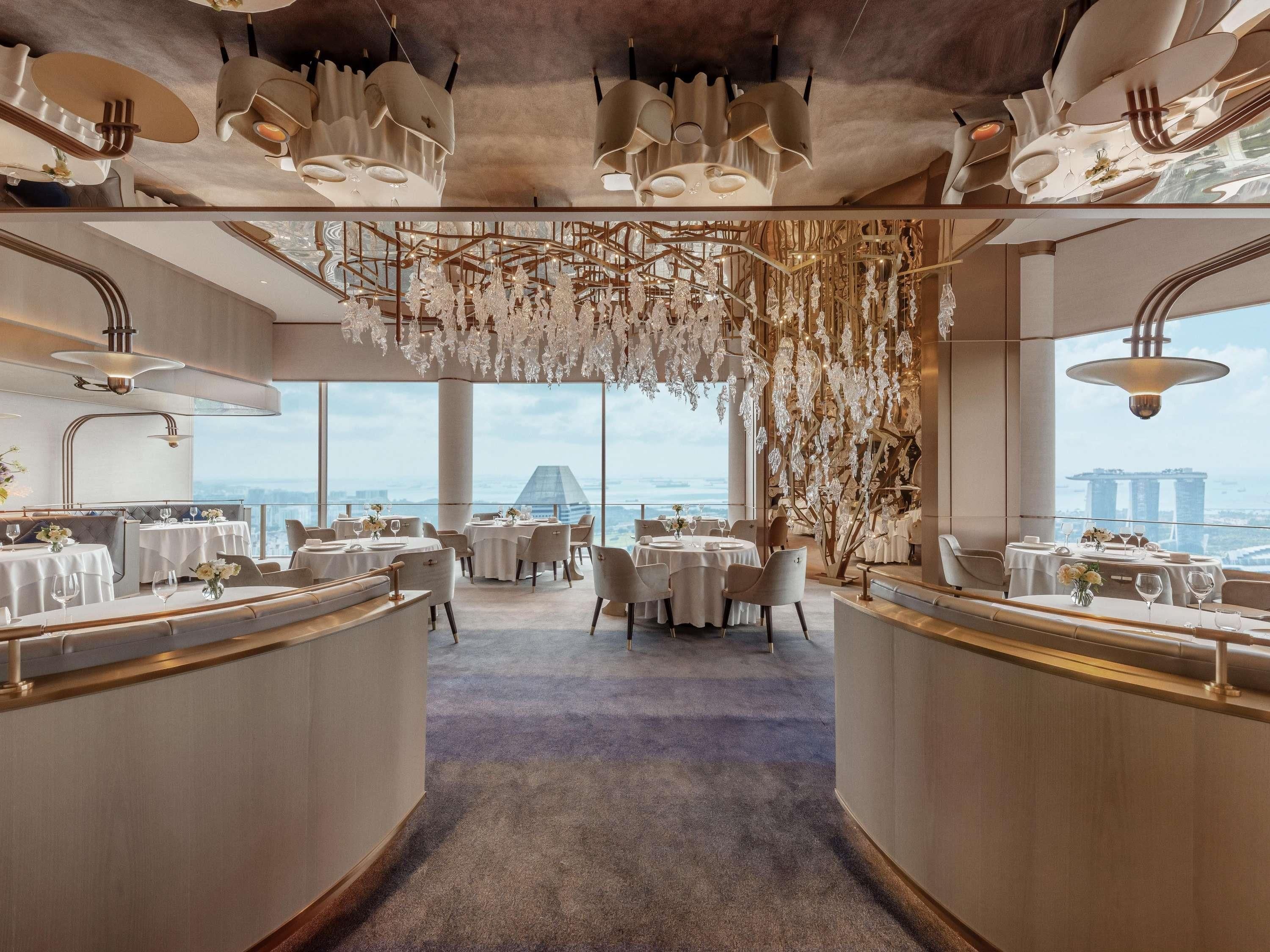 Um restaurante moderno com um bar central, mesas redondas e vista para o horizonte da cidade.