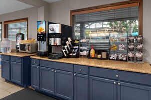 Um espaço com estação de café, dispensador de suco, máquina de café e dosadores de temperos.
