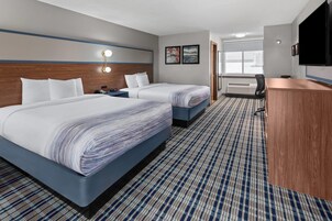 Quarto de hotel com duas camas, uma escrivaninha, uma cadeira, uma televisão de tela plana e uma janela com vista.