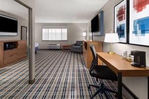 Quarto de hotel com uma cama, uma escrivaninha com cadeira, televisão, micro-ondas e máquina de café.