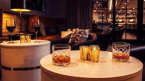Uma área de bar com mesas redondas, copos de uísque e um abajur.