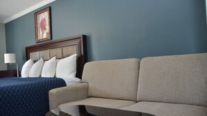 Quarto de hotel com cama, sofá, luminária e quadro na parede.