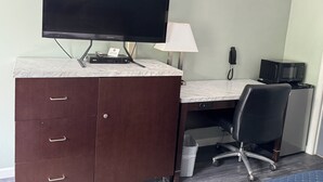 Quarto de hotel com televisão de tela plana, escrivaninha com luminária, telefone e micro-ondas.