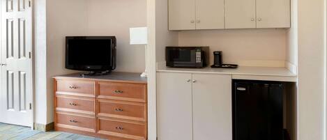 Quarto compacto com televisão, micro-ondas, frigorífico e cómoda de madeira.
