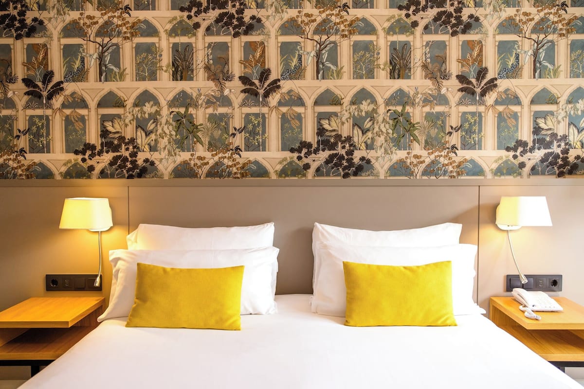 Quarto de hotel com uma cama grande, duas mesas de cabeceira e parede com padrão floral.