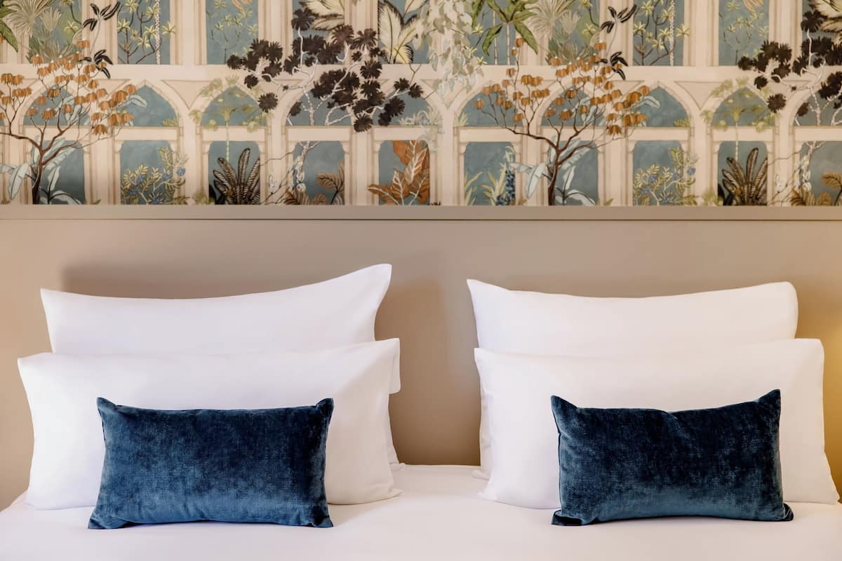 Uma cama com almofadas brancas e azul-escuras, uma tapeçaria floral e uma cabeceira branca.