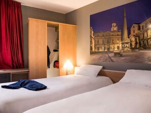 Quarto de hotel com cama, mesa de cabeceira, abajur, guarda-roupa e um mural na parede com vista para a cidade.