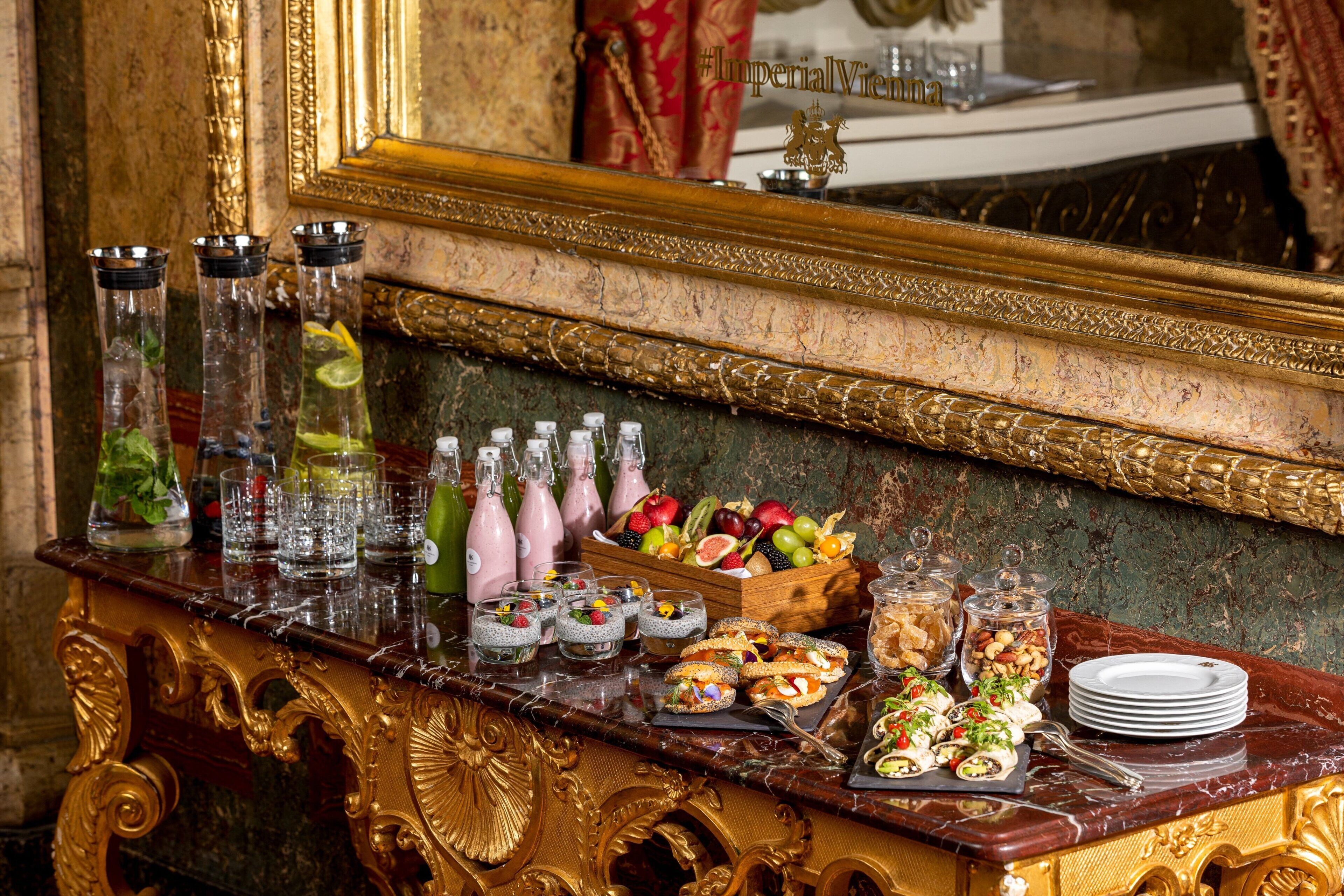 Uma mesa de buffet com diversos alimentos e bebidas, incluindo uma cesta de frutas e copos.