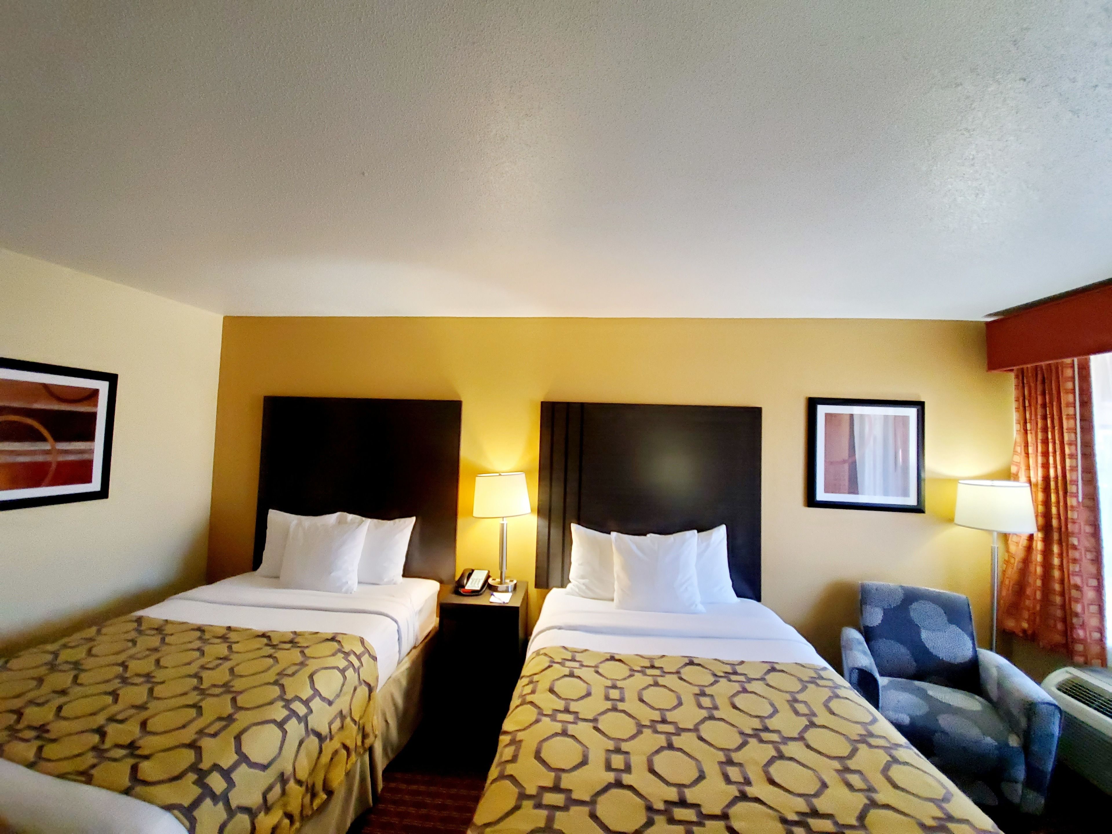 Quarto de hotel com duas camas, uma cadeira e uma mesa com abajur.