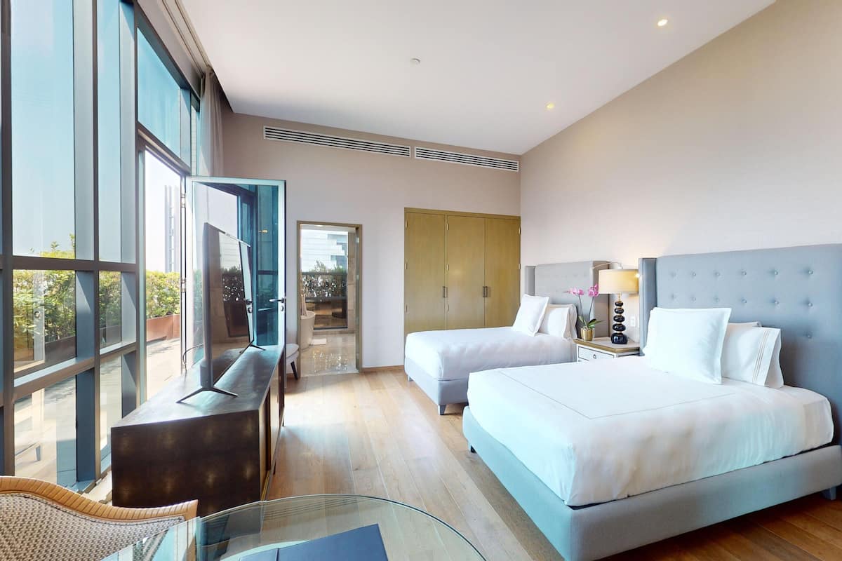 Quarto de hotel moderno com duas camas, uma mesa de trabalho e janelas amplas.