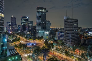 Vista noturna de uma cidade com arranha-céus modernos, uma rotatória e ruas iluminadas.