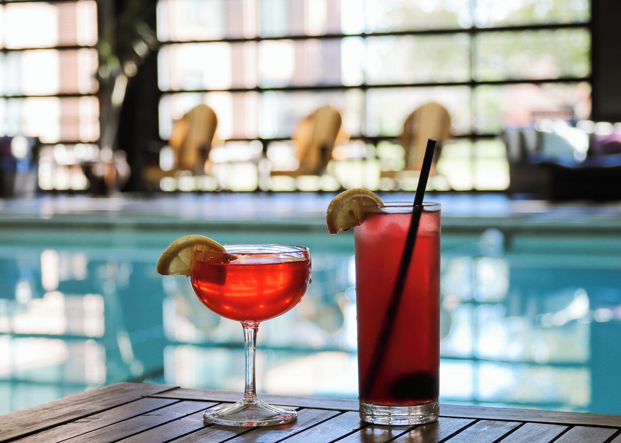 Duas bebidas sobre uma mesa de madeira à beira da piscina.