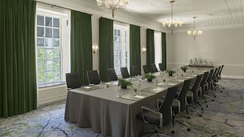 Uma sala de conferências com uma mesa comprida, cadeiras e cortinas verdes.