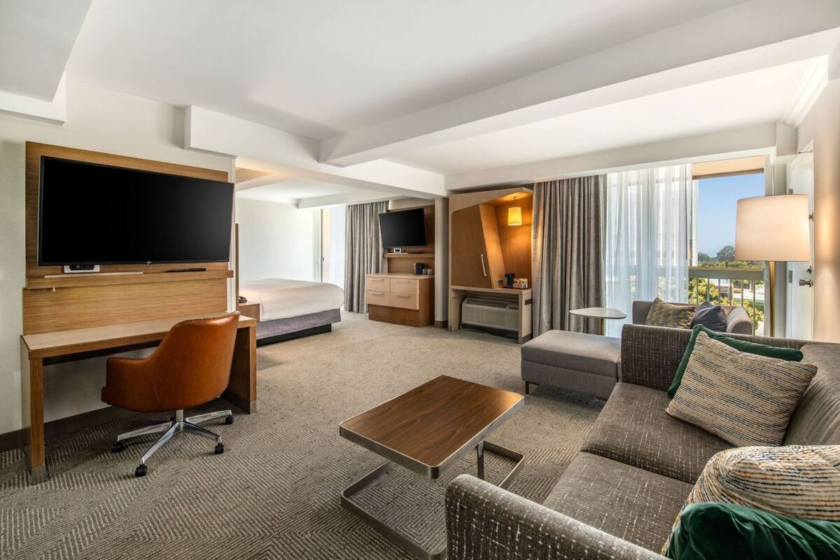 Quarto de hotel moderno com televisão de tela plana, escrivaninha, sofá confortável e cama.