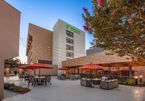 Uma área de pátio ao ar livre com mesas e cadeiras, luzes de corda e um edifício com uma placa que diz 'Holiday Inn Express'.