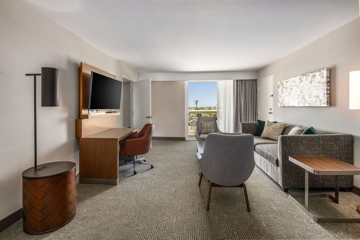 Quarto de hotel com televisão de ecrã plano, secretária, sofá e vista para o exterior.