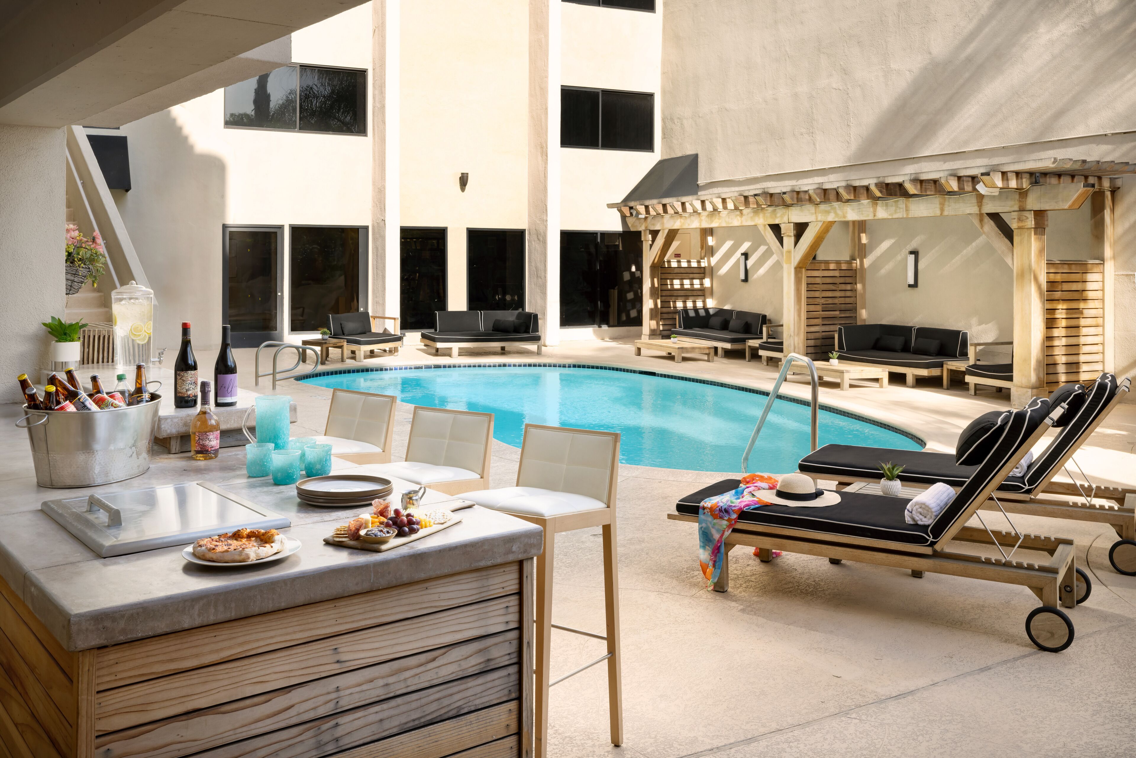 Uma área à beira da piscina com espreguiçadeiras, um bar com dispensador de bebidas e a piscina.