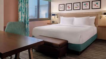Quarto de hotel com uma cama, uma escrivaninha, uma cadeira e uma janela com cortinas.