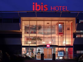 Um hotel moderno com uma placa grande de "ibis HOTEL", amplas janelas de vidro e uma entrada bem iluminada.