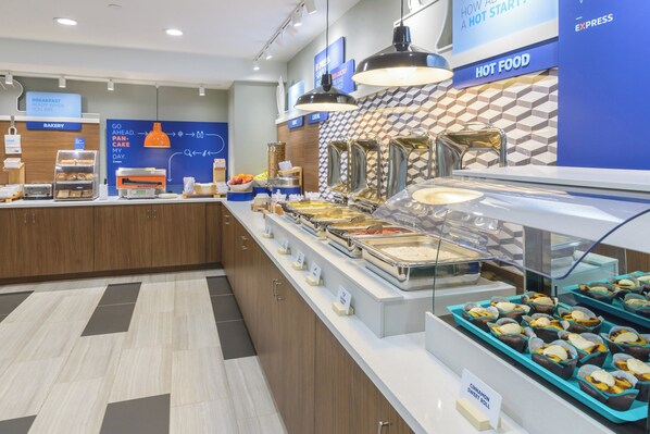 Espaço de buffet de café da manhã com diversas opções de alimentos e uma seção de padaria.