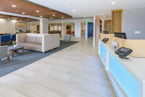Um hall de hotel com balcão de recepção, área de estar e espaço para refeições.