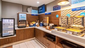 Espaço do buffet de café da manhã com seções identificadas para ovos, leite, cereais, frutas e comida quente.